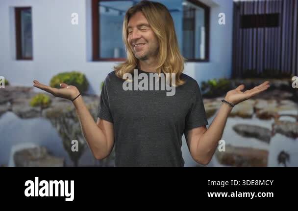 Blond man stands at house entrance door with open palms facing outward ...