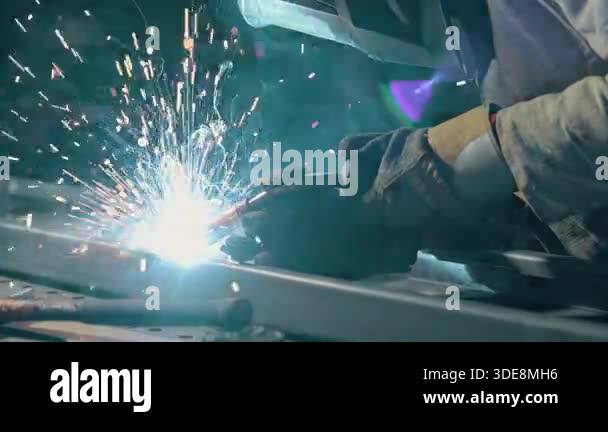 A close-up of a worker welding metal, with bright sparks flying as the ...