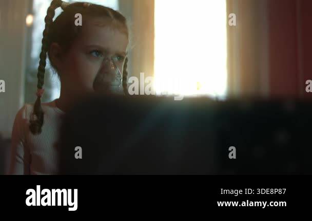 Sick child is holding a nebulizer mask herself and watches cartoons for ...