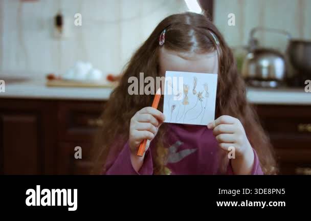 Small girl is hiding behind her pencil drawing, then shows her smiling ...