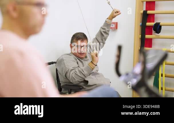Overweight man in a wheelchair working on his arm and back muscles ...