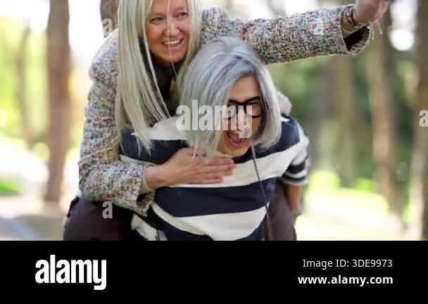 Two joyful senior women friends having fun together outdoors. One woman ...