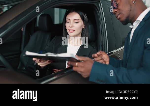 Woman with dark hair is seated in a car, smiling and engaging with a ...