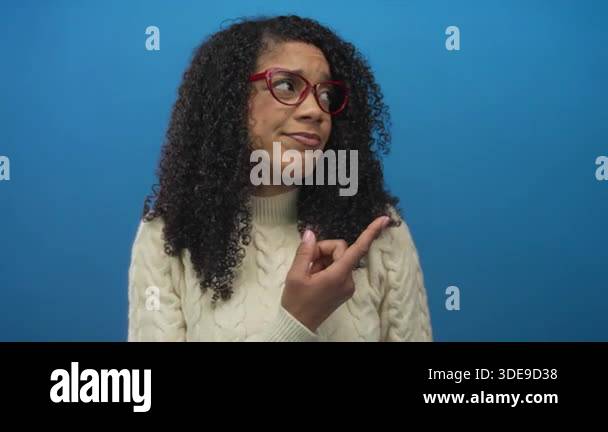 Woman with curly hair and red glasses points finger sideways in studio ...