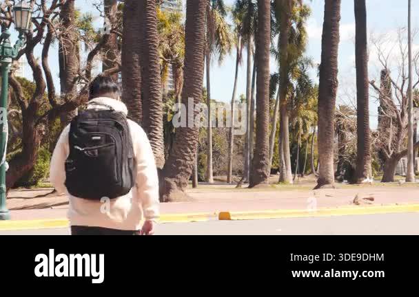 Man walking with a backpack through a palm lined park illustrating ...