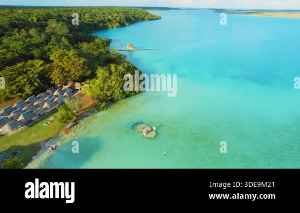 Thatched huts along Bacalar Lagoon shoreline by green tropical forest ...