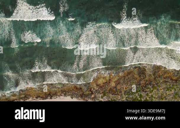 Tidal ocean waves crash onto rocky coastal reef from aerial top view ...