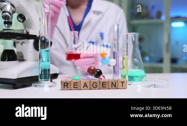 Lab worker holds transparent glass beaker and uses pipette to draw up ...