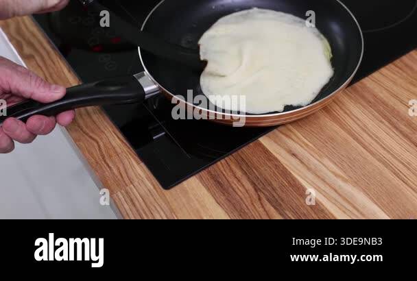 Man holds handle trying to flip thin pancake in frying pan. Male cooks ...