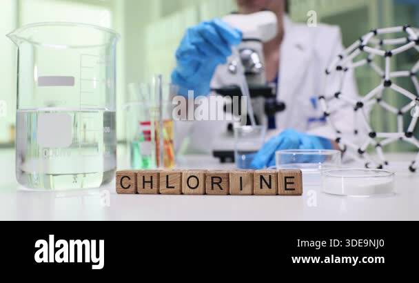 Wooden cubes on desk spell word Chlorine near clear beaker and rack ...