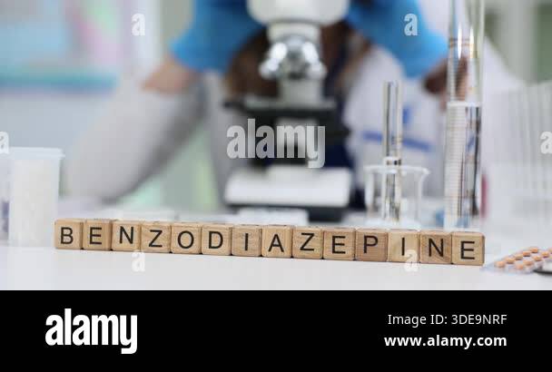 Wooden blocks on desk spell word Benzodiazepine beside glassware. Woman ...