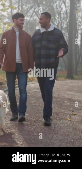 two men walking dog in park white man and black man holding hands while ...