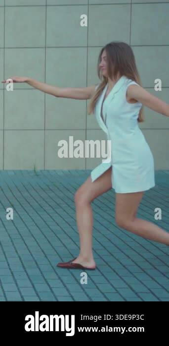 Playful white woman dancing on pavement, tiled wall backdrop, summer ...