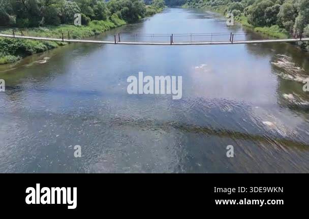 Aerial view of a suspension footbridge spanning a calm river with ...