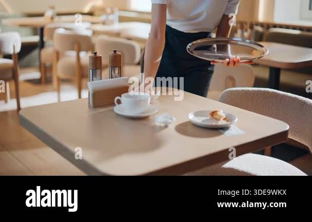Closeup waitress cleaning table taking plates at empty light cafeteria ...