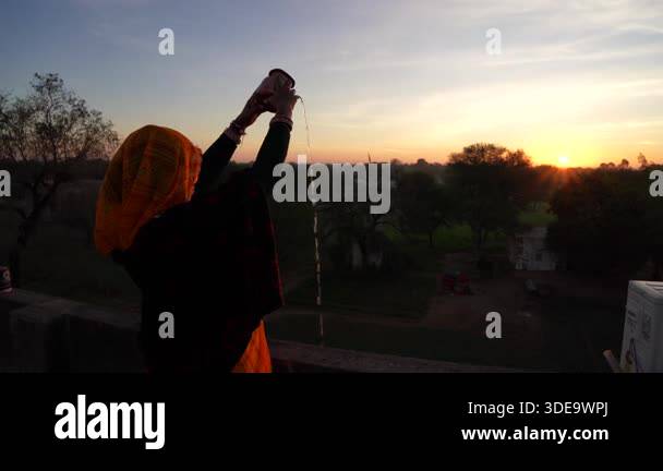 Indian woman in sari offering water to the Sun God during a traditional ...