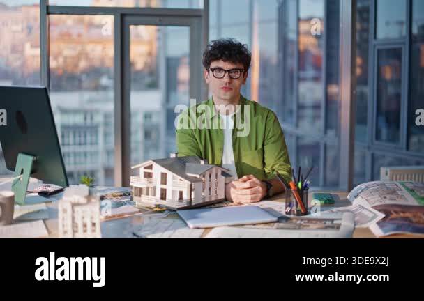 Real estate developer smiling in camera sitting desk with blueprints ...