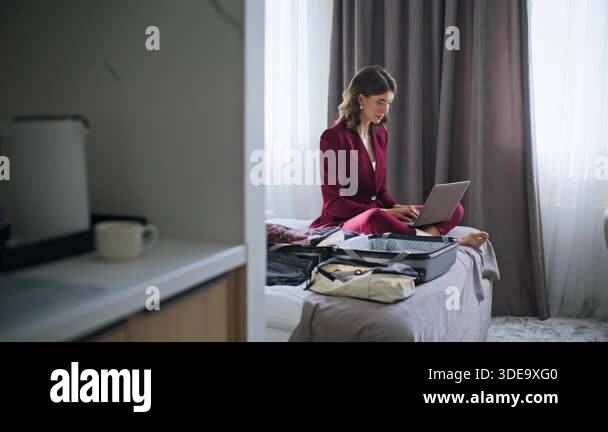 Stylish brunette typing laptop sitting cross-legged at hotel bed ...