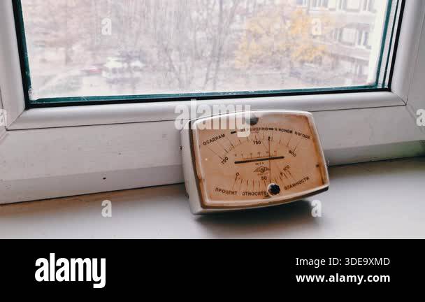 A vintage analog barometer stands on a white windowsill against a ...