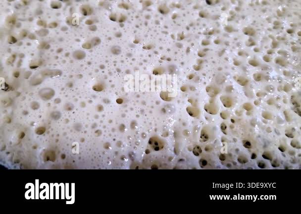 Macro close-up of pancake batter cooking in a pan. Bubbles continuously ...