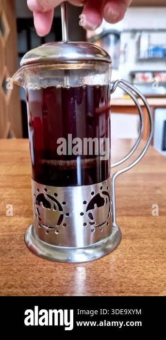 Vertical, medium shot of a hand pressing the plunger of a French press ...