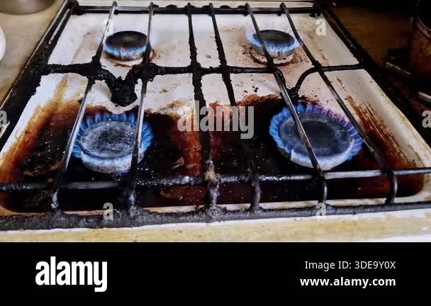Wide shot of a dirty white gas stove with three burners lit, showing ...