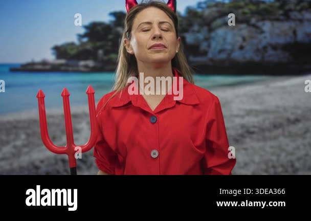 Woman smiles brightly and holds red trident beside her face in studio ...
