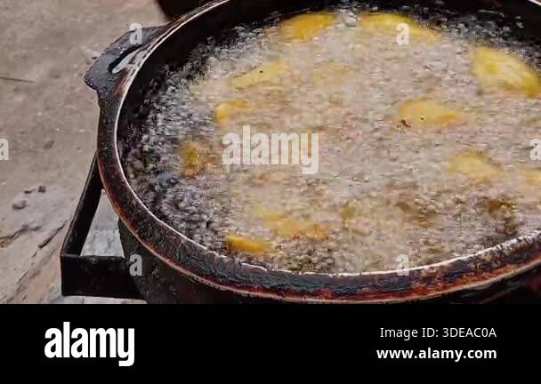 Close up view of deep frying plantain in old metal saucepan with dark ...