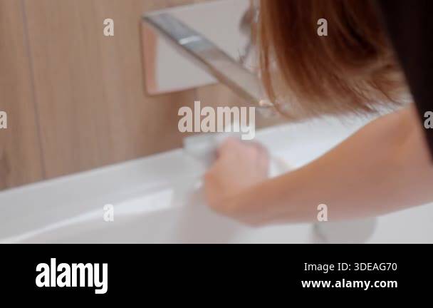 Woman cleaning bathtub with modern faucet, wiping dust in bathroom ...