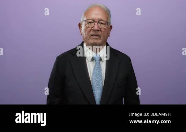 Senior man in business suit points upward against an isolated purple ...