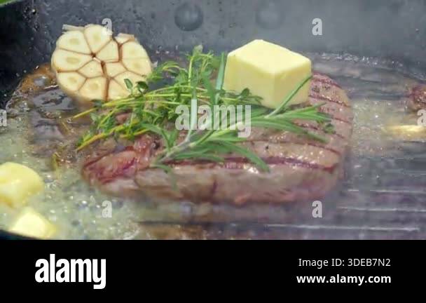 seared steak topped with herb sprigs, garlic bulb and melting butter on ...