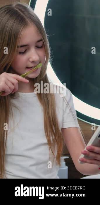 Cute little girl brushing teeth and using smartphone checking social ...
