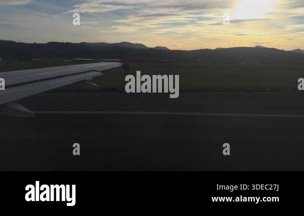 At sunset, an airplane taxis as its wing silhouettes over runway lines ...