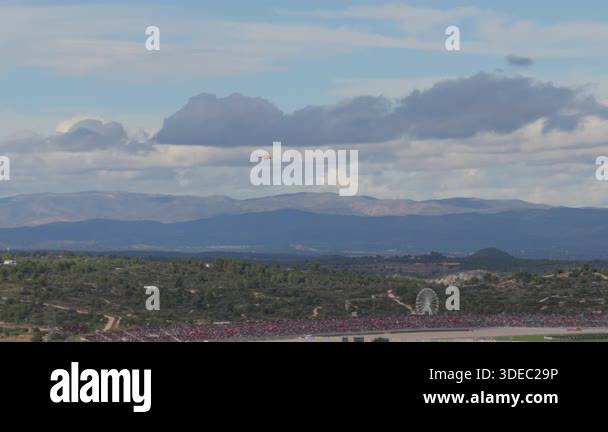 An orange stunt plane flies across a bright sky over a crowded rural ...