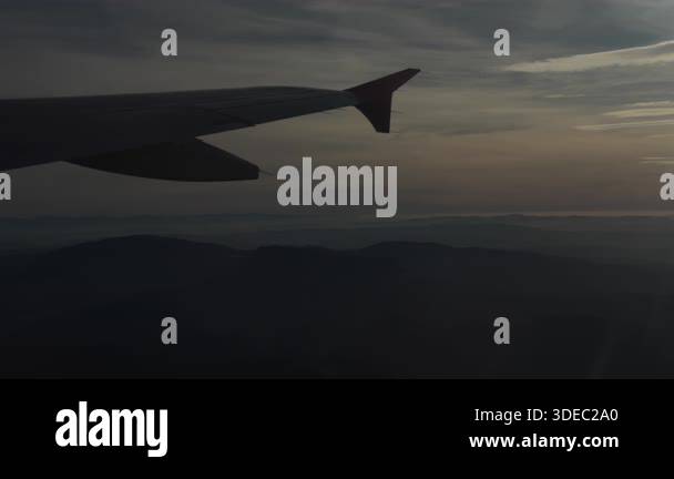 Serene airplane window scene: jet wing over layered mountains at golden ...