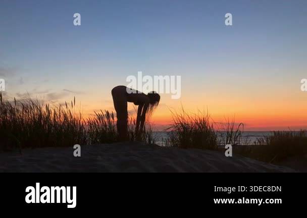 Silhouette of a person bending in a yoga pose on a sandy beach at ...