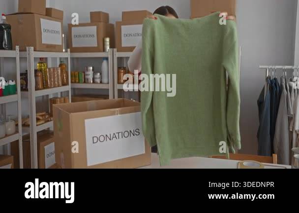 Woman volunteering at donation center sorting clothes among boxes and ...
