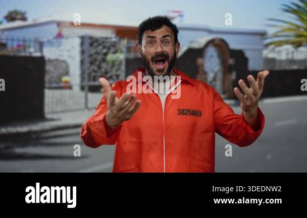 Hispanic man with beard in an orange prison jumpsuit stands outdoors on ...