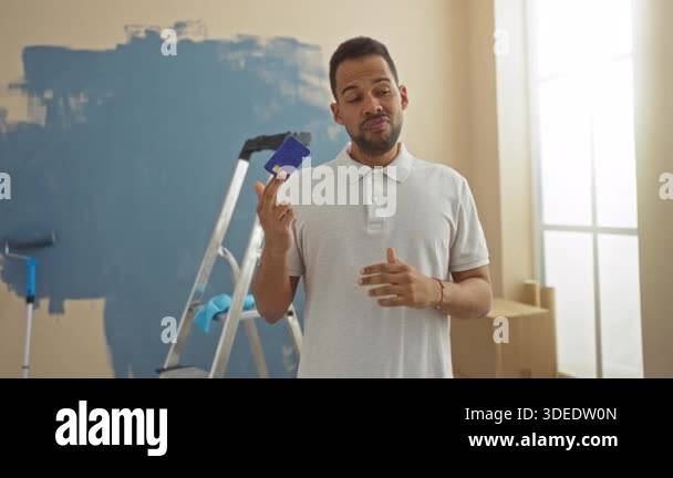 Young man holding credit card inside new home with paint roller ladder ...