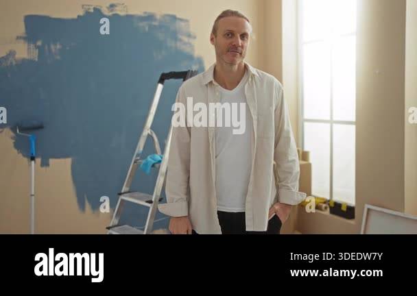 Man painting home interior with paint roller near ladder and window in ...