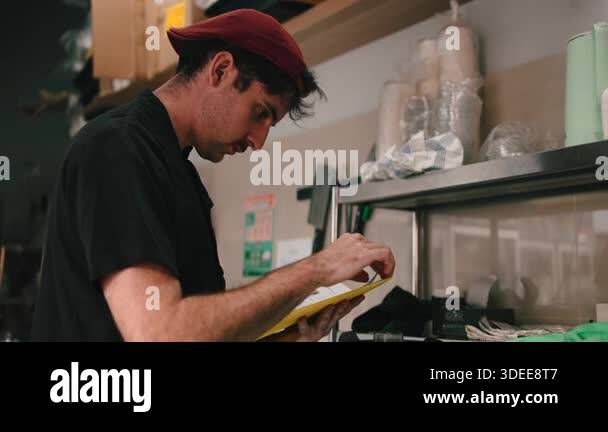 Focused chef in a commercial kitchen meticulously checking a list of ...