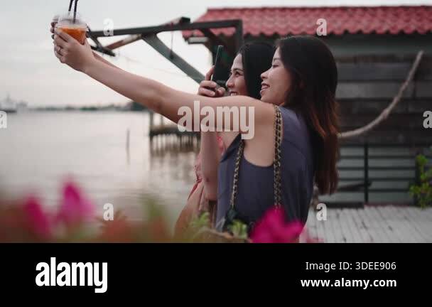 Two young asian women having fun taking a selfie with their drinks at a ...