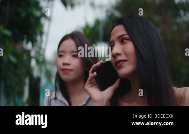 Two young asian women hanging out together in a park while one is ...