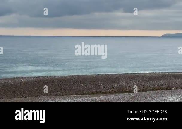 A calm beach scene with a pebbled shore and gentle waves. The sky is ...