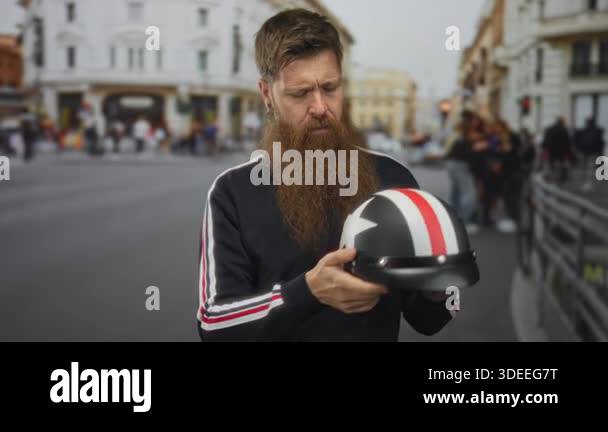 Young man with long beard holding a black and white striped motorcycle ...
