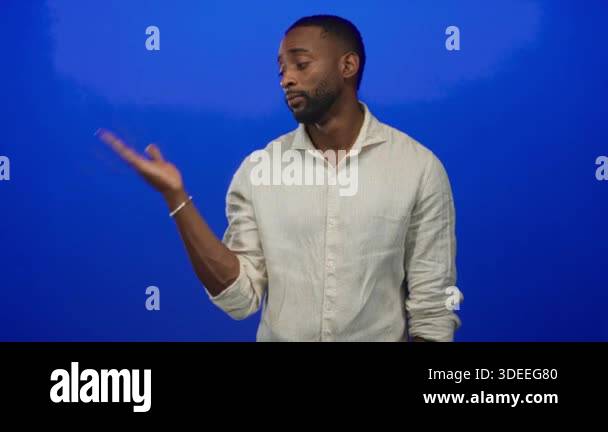 Man presenting open left palm in studio with solid blue wall, casual ...