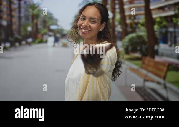 Young african american woman reaching hand toward camera on street with ...