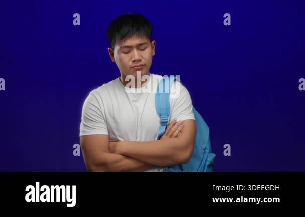 Young man with arms crossed wearing blue backpack isolated against blue ...