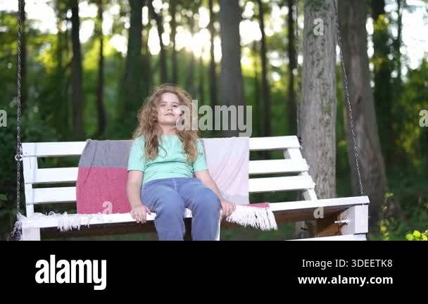 Relaxed child on wooden swing. Cozy rest on garden swing. Kid sitting ...