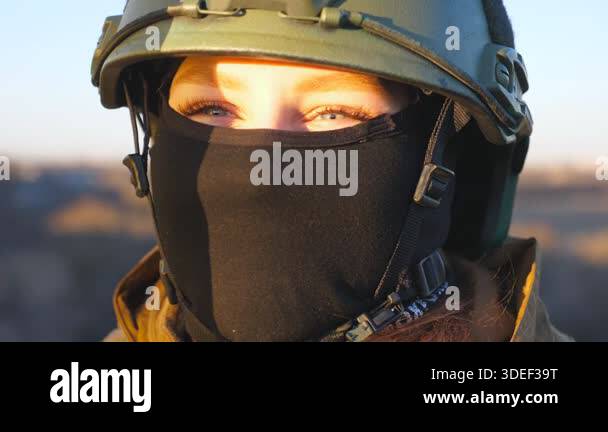 Portrait of young military woman in helmet and balaclava at countryside ...